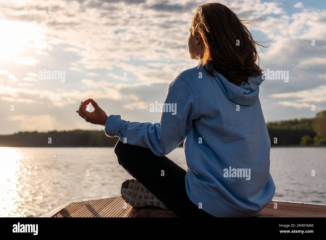 Rear view brunette woman sitting on lake pier in lotus position ...
