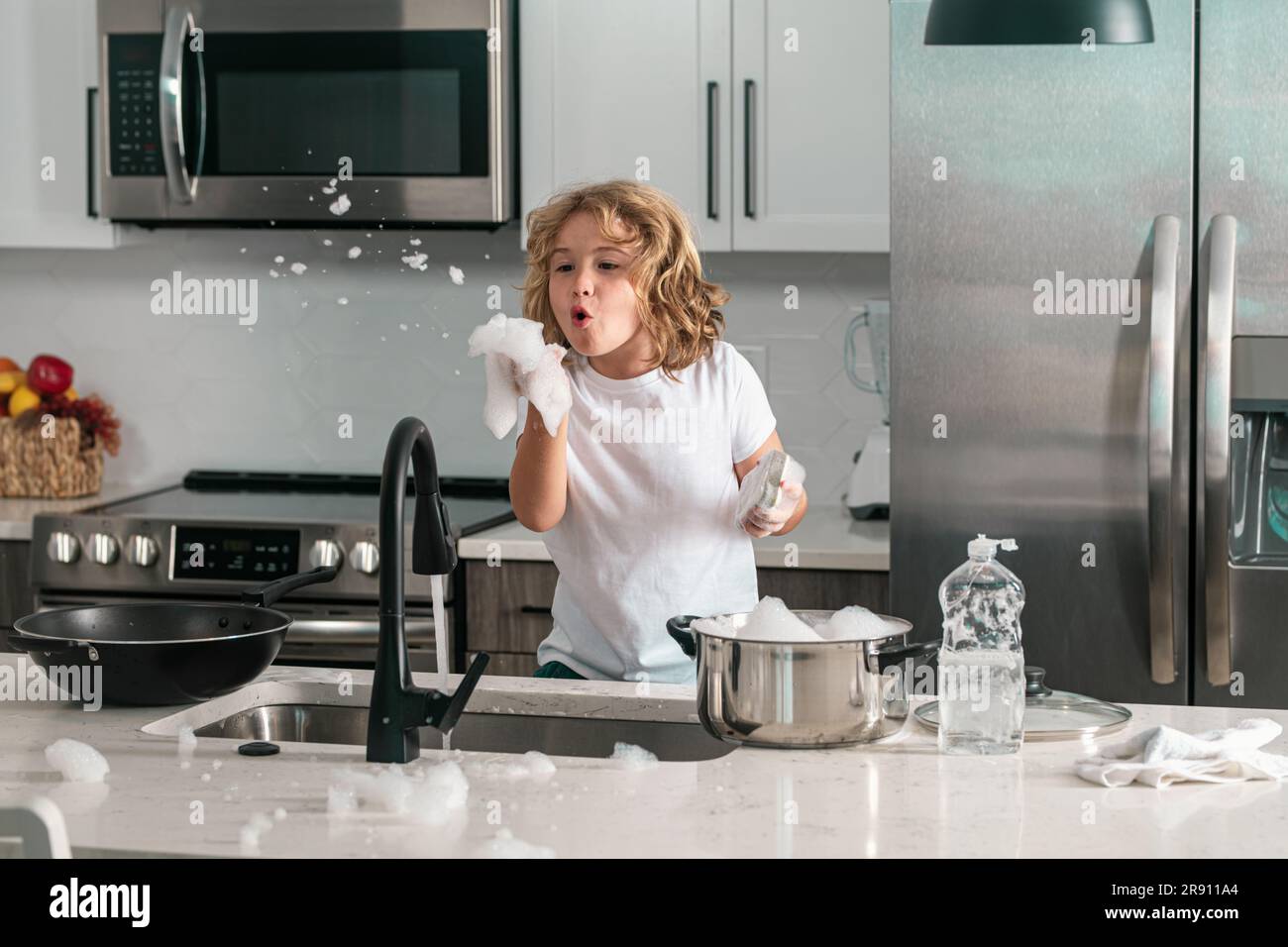 Child washing dishes near sink in kitchen. Child with sponge with dish ...