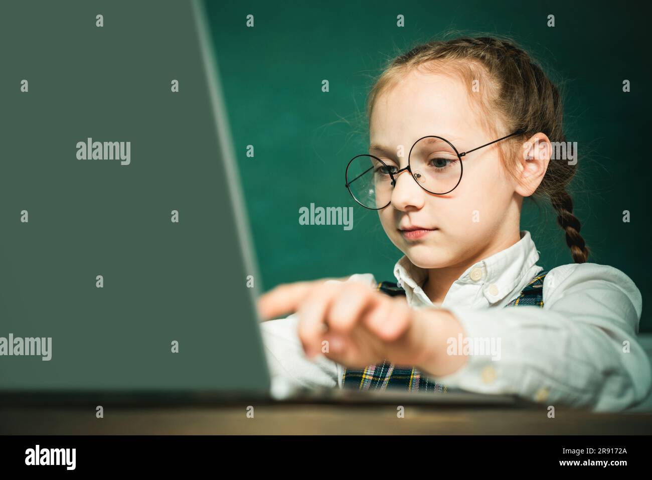 Pupil working on laptop computer over blackboard background. Child near ...