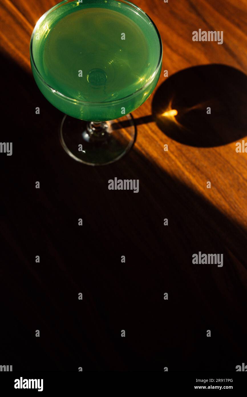 green absinthe drink in a coupe glass with on wooden table in the sun ...