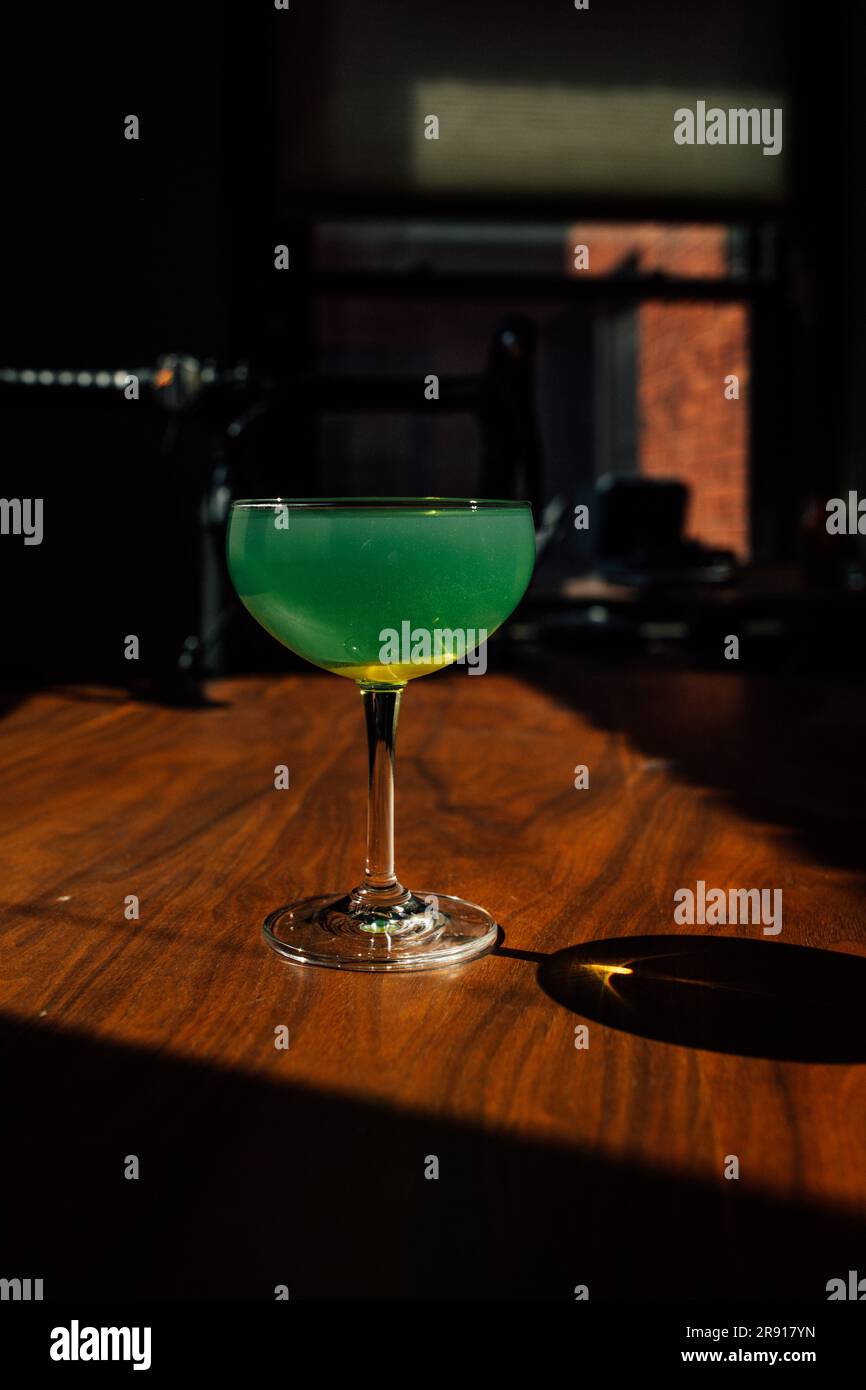 green absinthe drink in a coupe glass with on wooden table in the sun ...