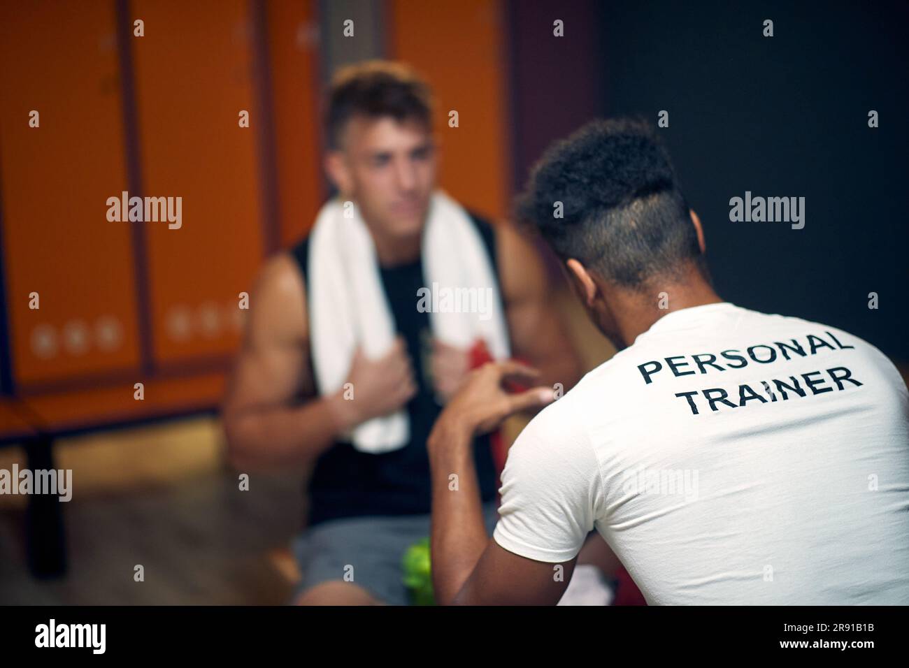 Coach advising young boxer in dressing room, sitting on becnh facing ...