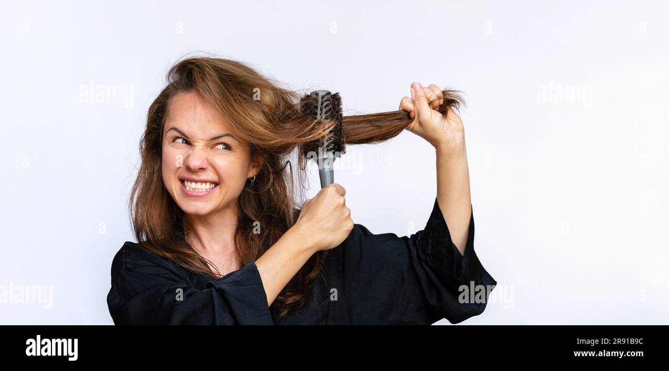 Annoyed angry brunette woman unsuccessfully trying to style her hair ...