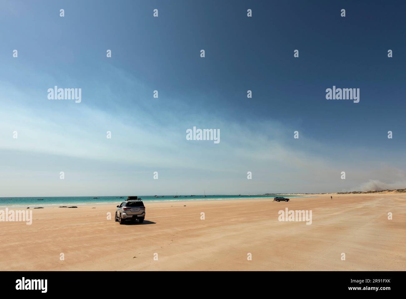 Cars parked on the long flat beach while boats are anchored of shore on ...