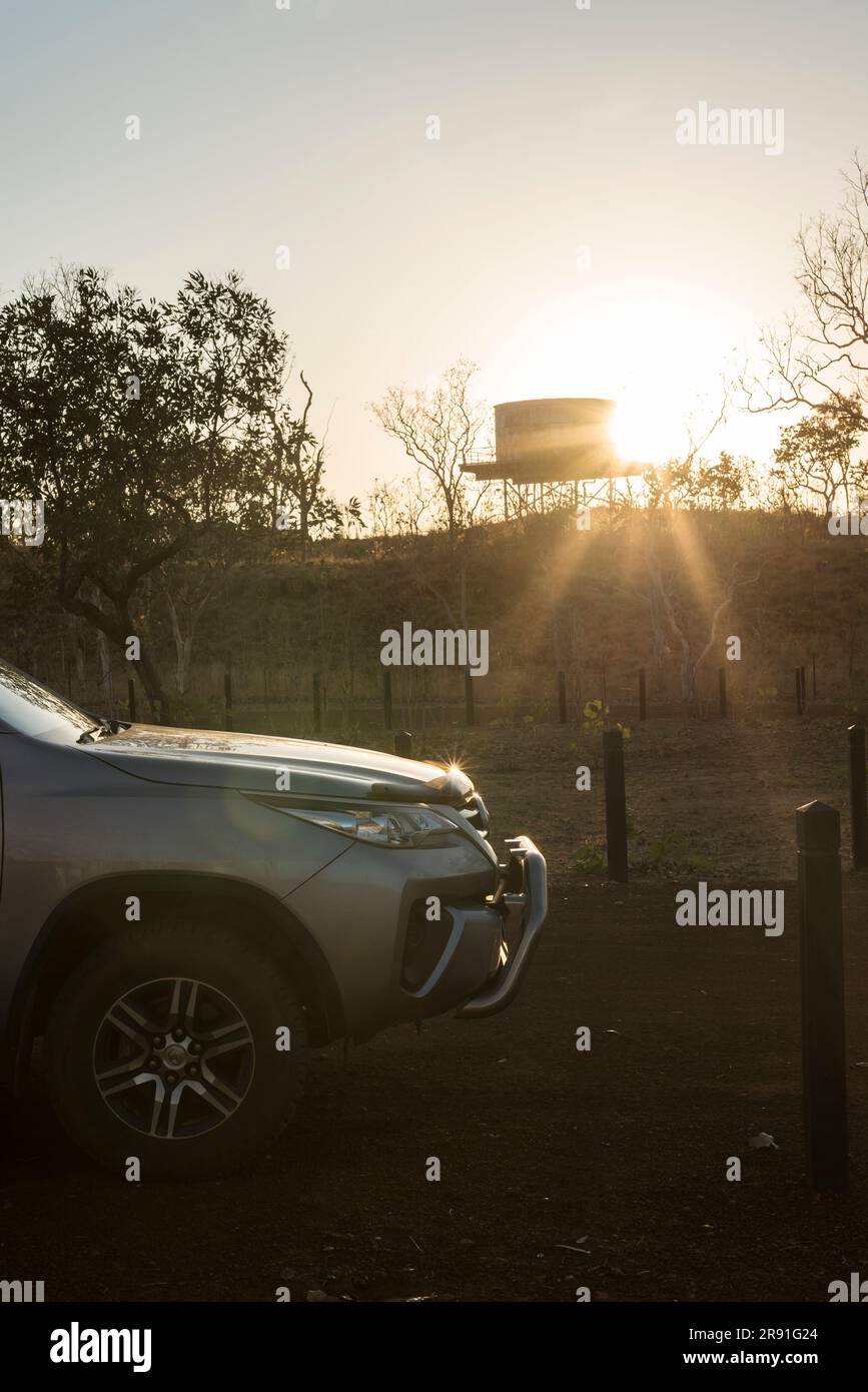 The sun sets behind a large water tank on a hill near a campground in ...