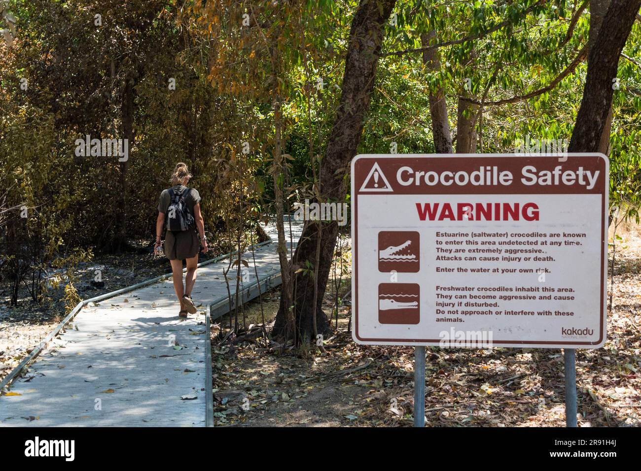 A woman walks passed a crocodile warning sign in Kakadu National Park ...