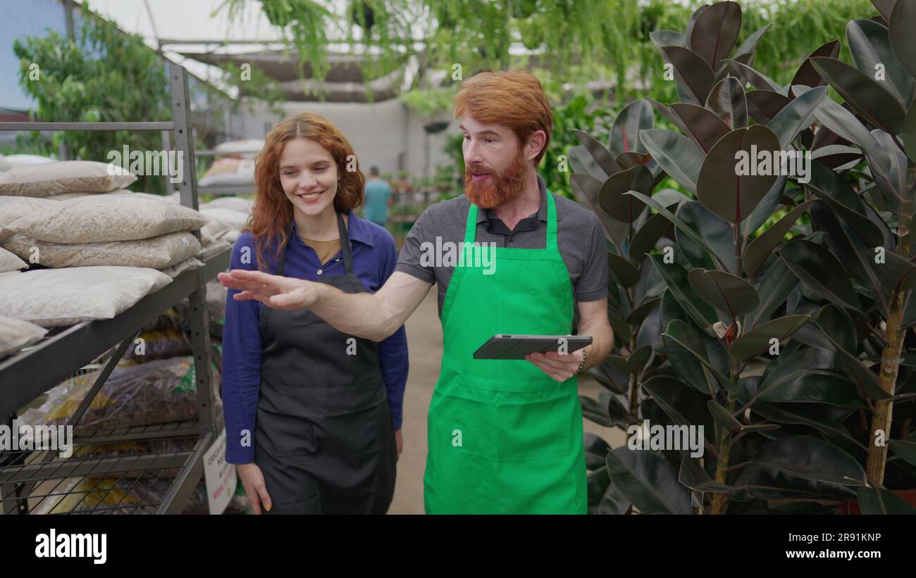 A male staff showing inventory to female colleague at local plant shop ...