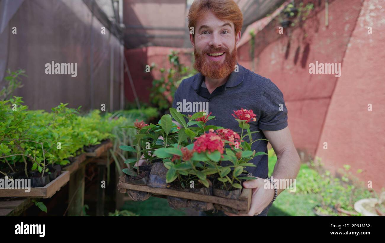 Joyful young man pulling plant from shelf standing outside in backyard ...