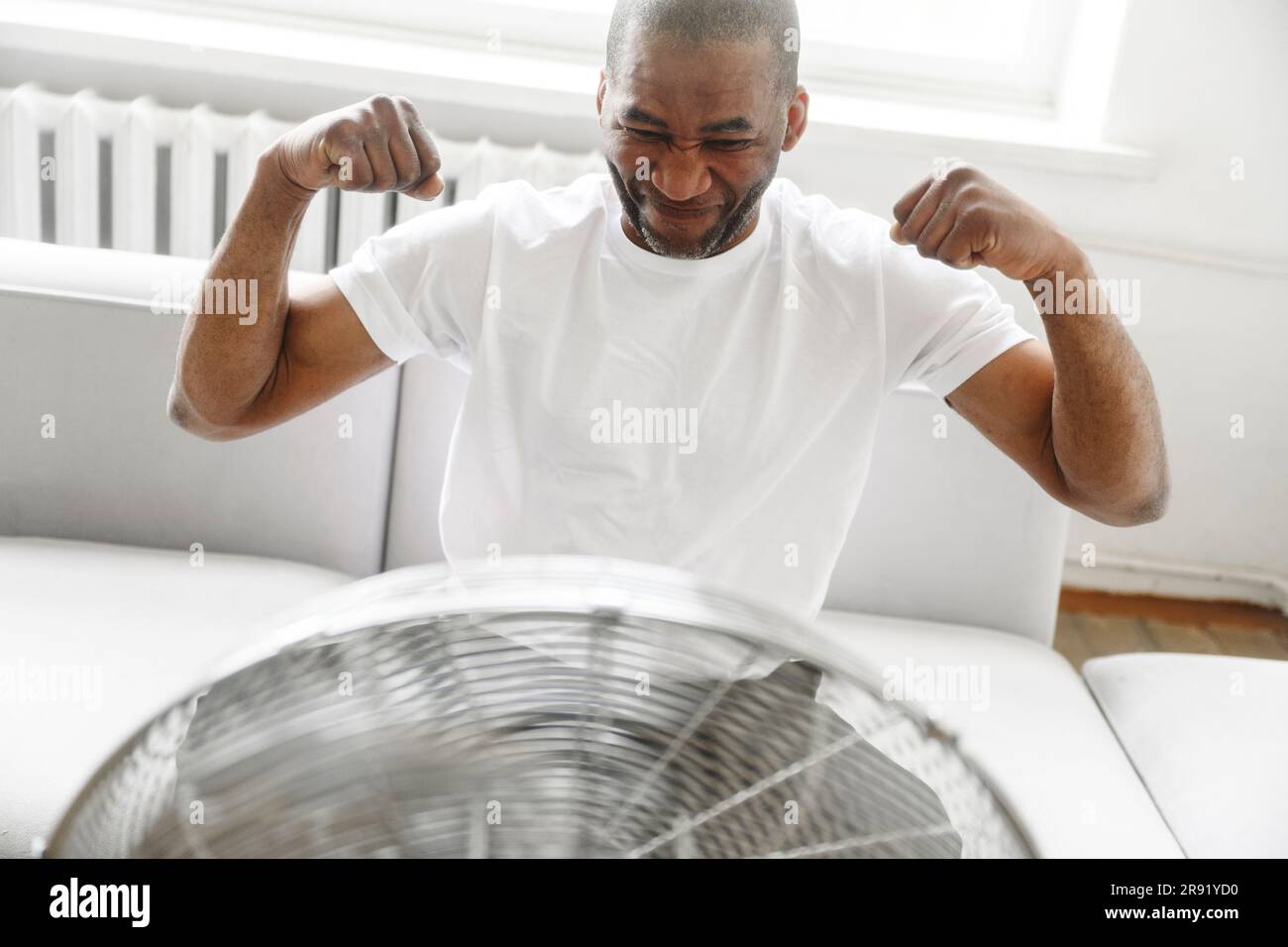 Man flexing muscles in front of electric fan at home Stock Photo - Alamy