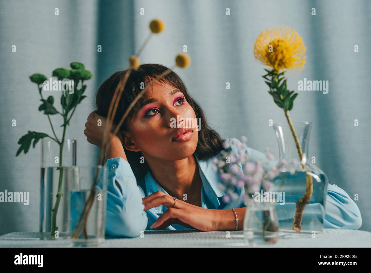Thoughtful woman sitting at table with flowers in front of blue ...