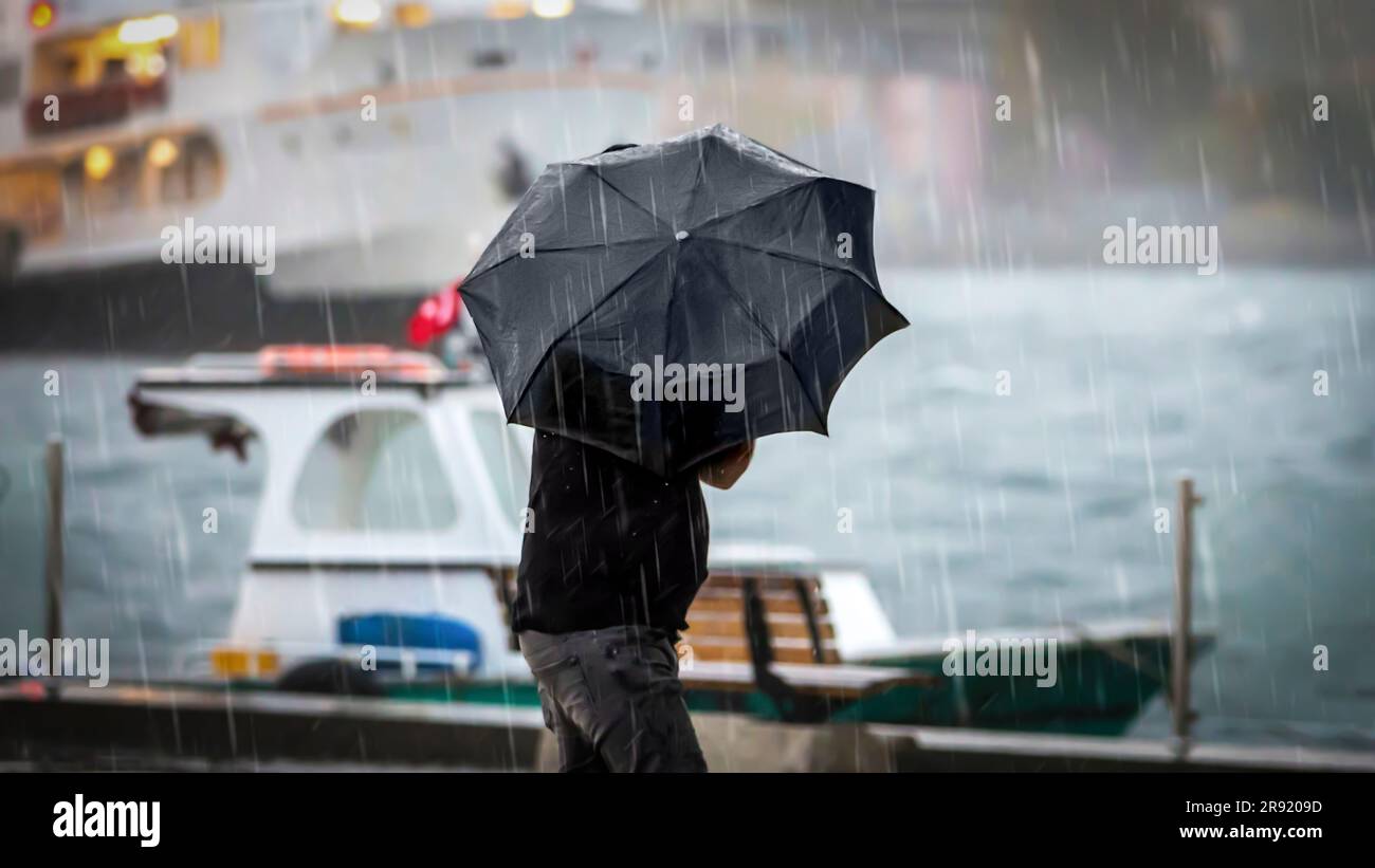 A man with an open umbrella in hand stands on a wooden boat dock in a ...