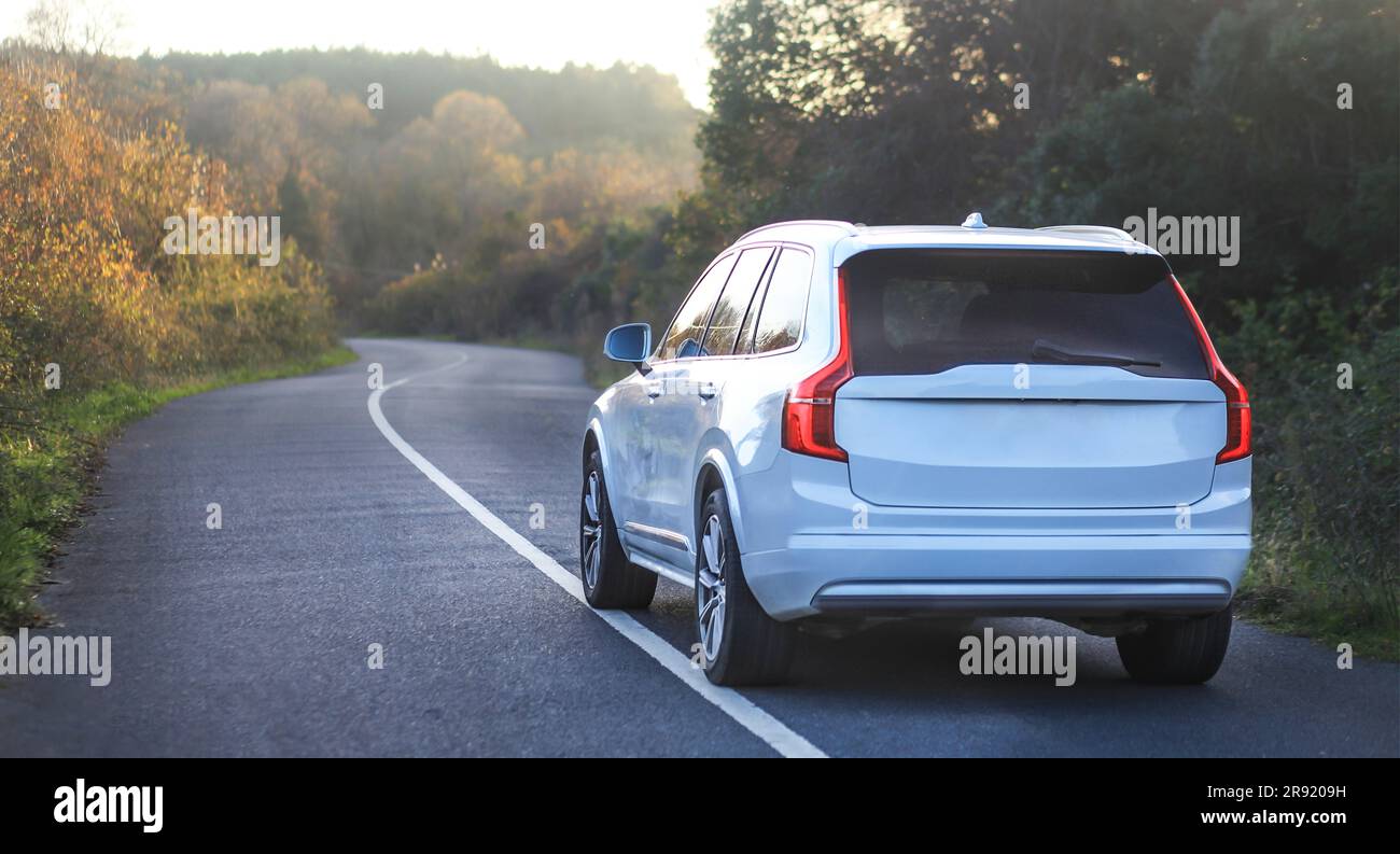A white car driving down a winding tree-lined road, shining in the ...