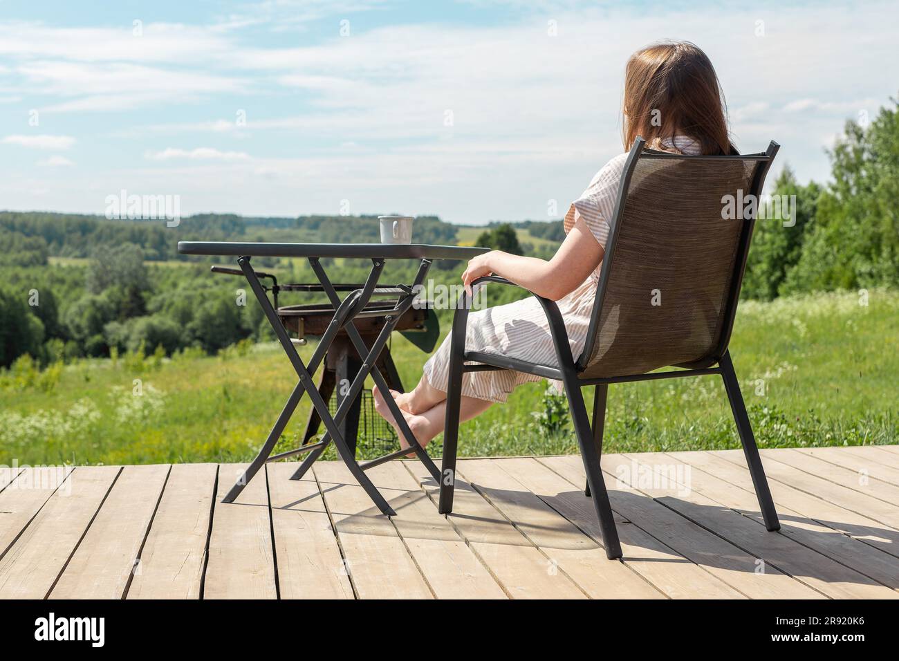 Woman relaxing on terrace, sitting in chair at table, enjoying view on ...