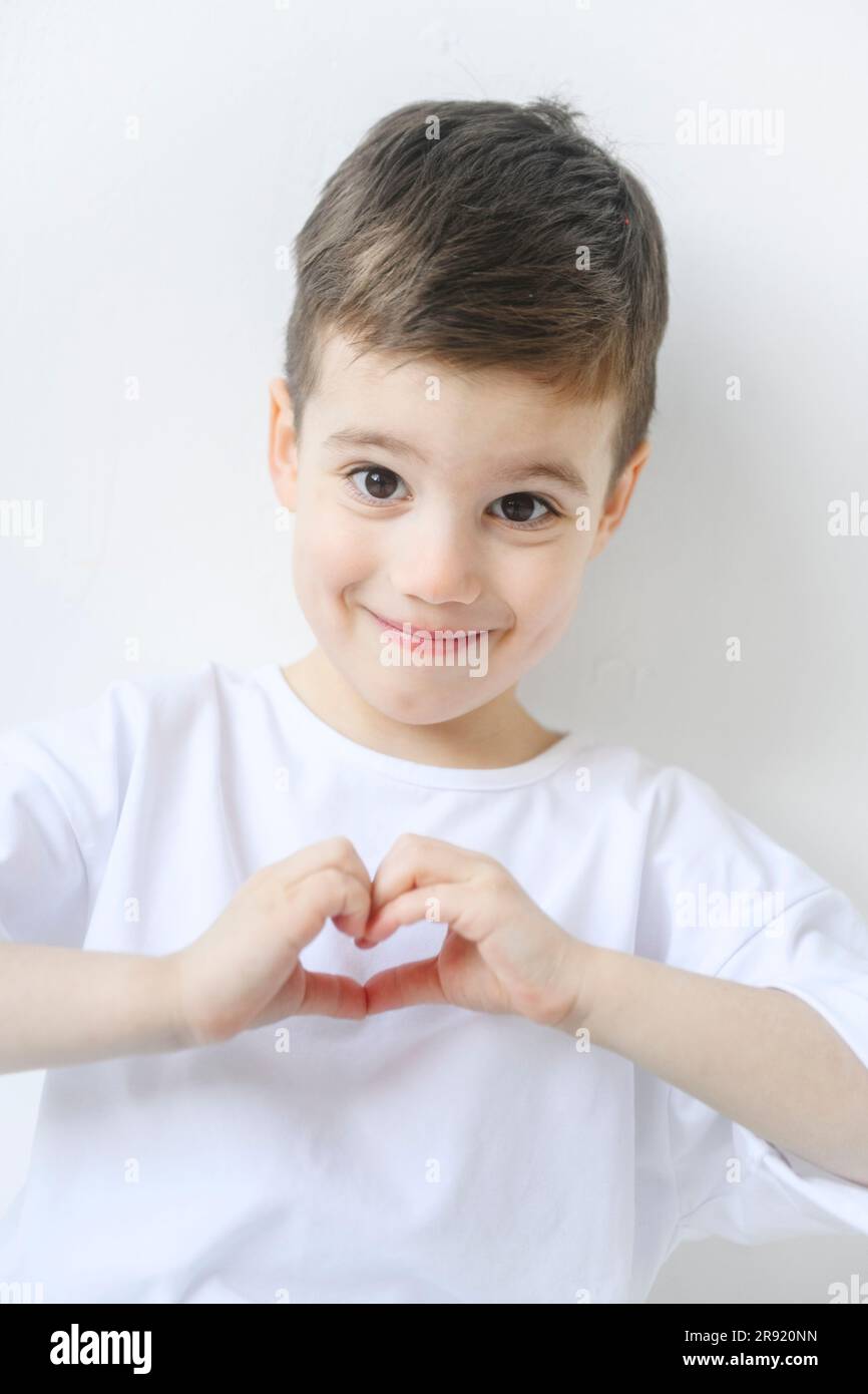 Smiling boy making heart gesture against white background Stock Photo ...