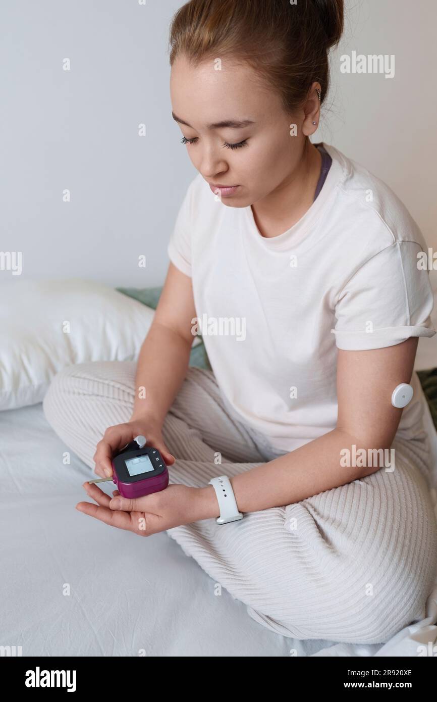 Woman with diabetes sitting on bed holding glucometer at home Stock ...