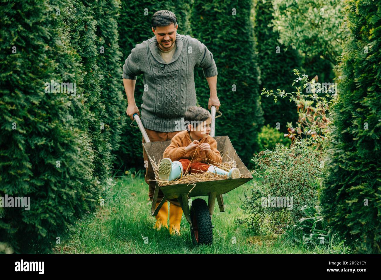Father pushing son sitting on hay in wheelbarrow at back yard Stock ...