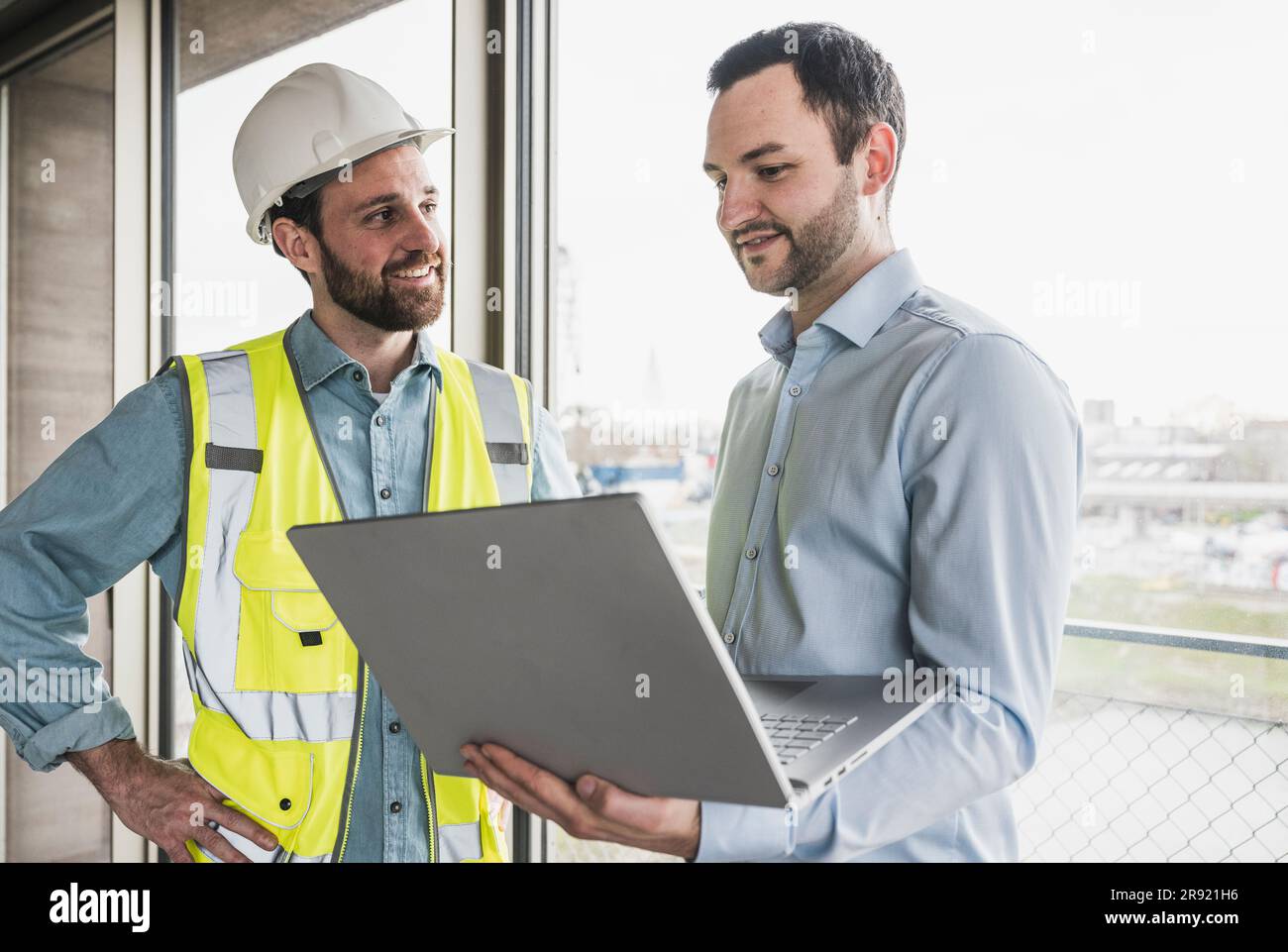 Smiling building contractor looking at architect holding laptop Stock ...