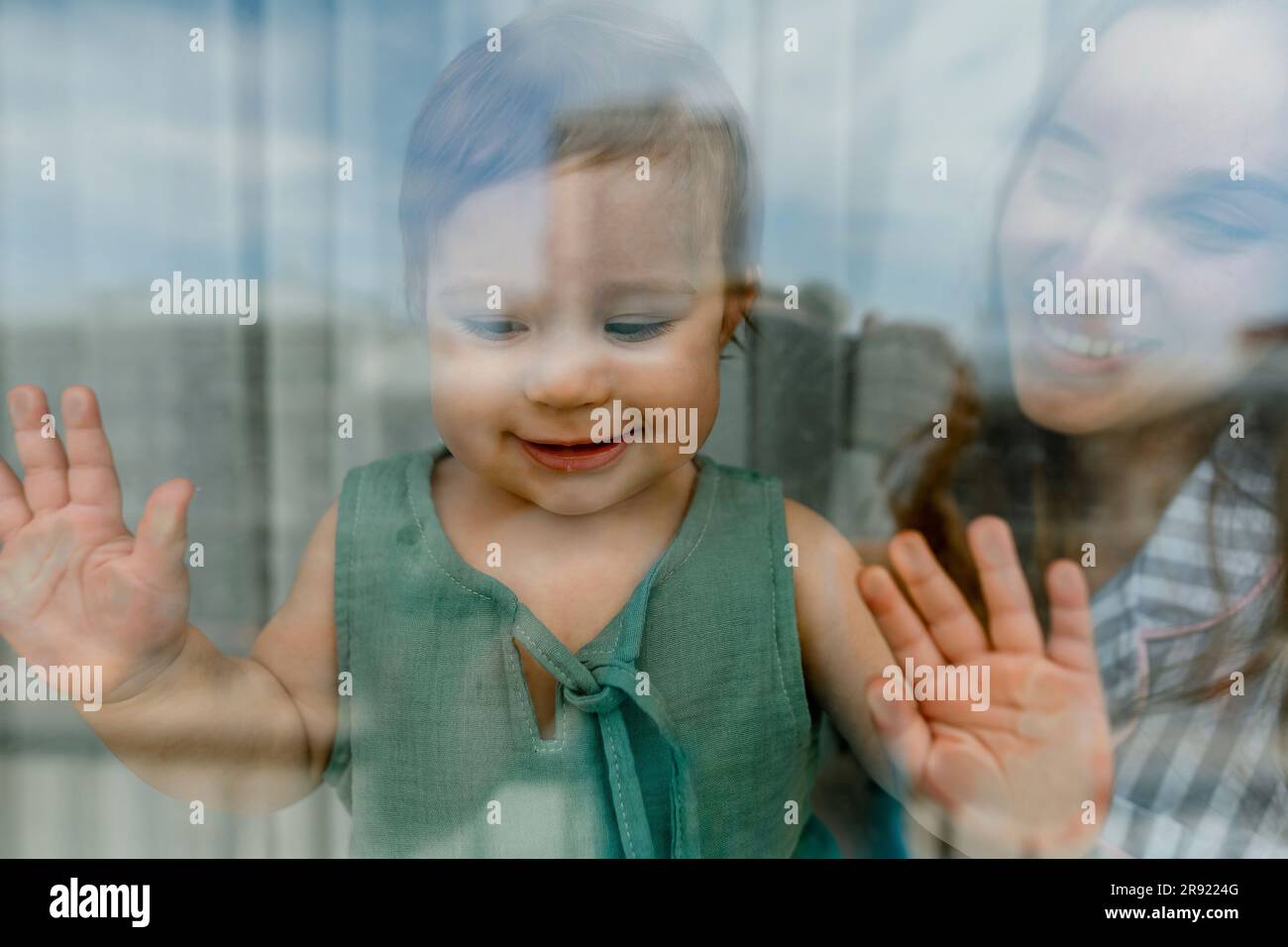Mother with baby girl looking out of glass window Stock Photo - Alamy