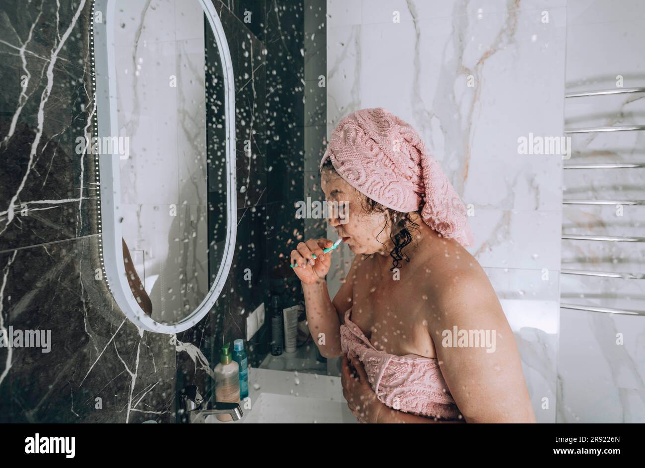 Woman wrapped in towel brushing teeth in bathroom Stock Photo - Alamy
