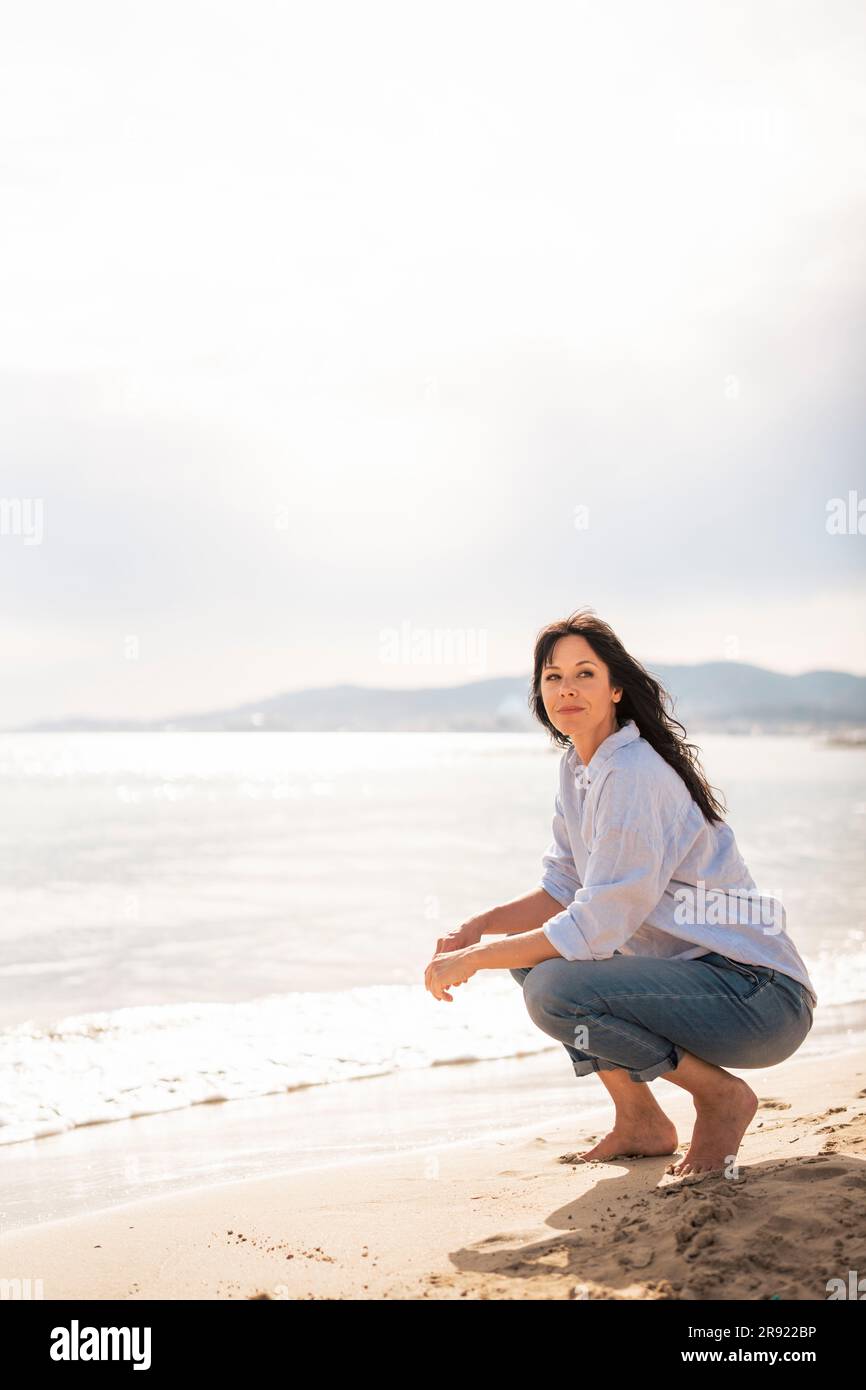 Mature Woman Spending Leisure Time Crouching On Sand At Beach Stock