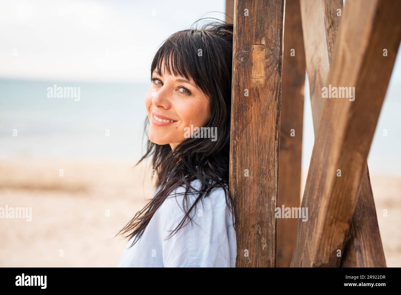 Smiling woman leaning on lifeguard hut at beach Stock Photo - Alamy