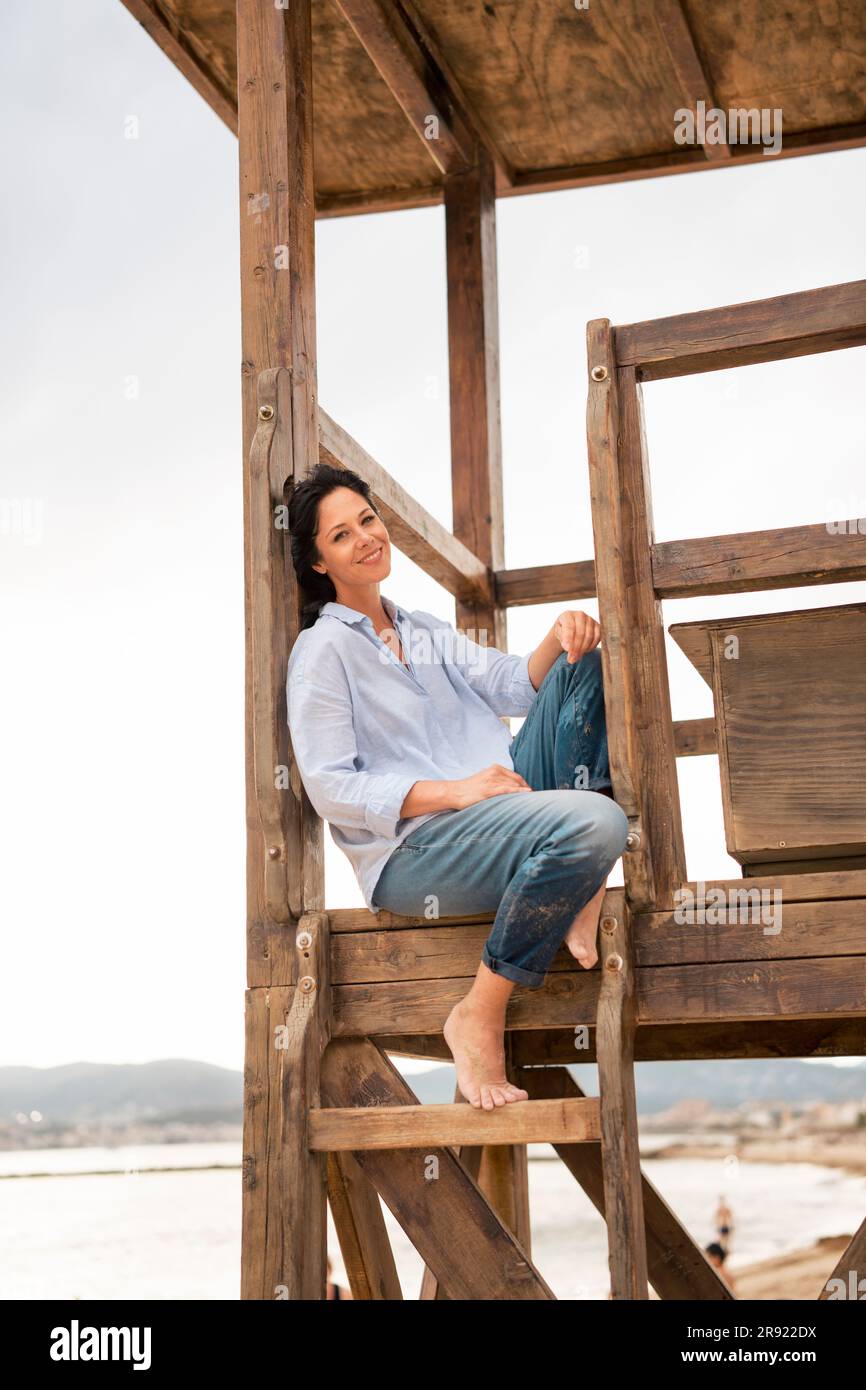Mature smiling woman sitting on lifeguard hut at beach Stock Photo - Alamy