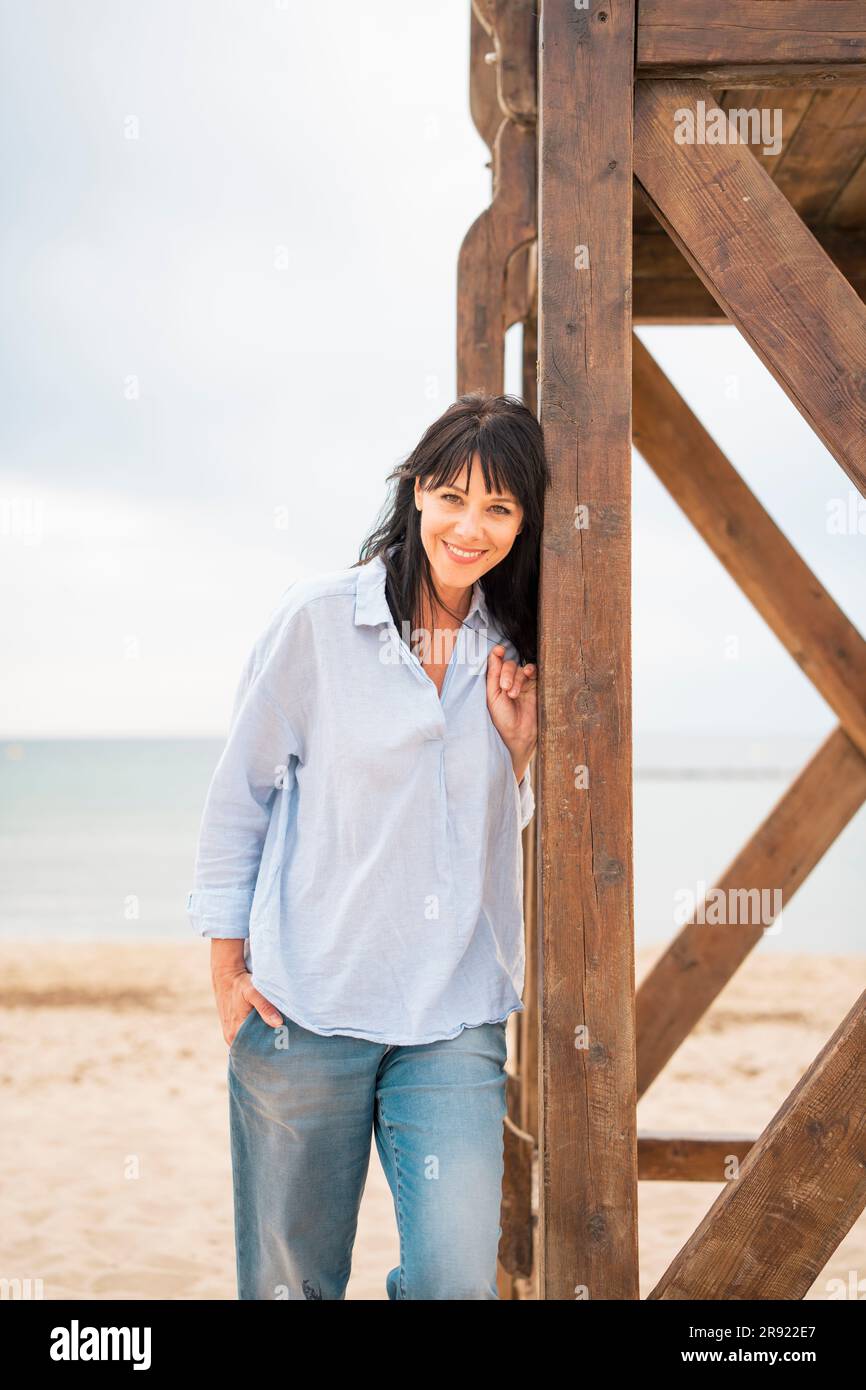 Smiling mature woman by lifeguard hut at beach Stock Photo - Alamy