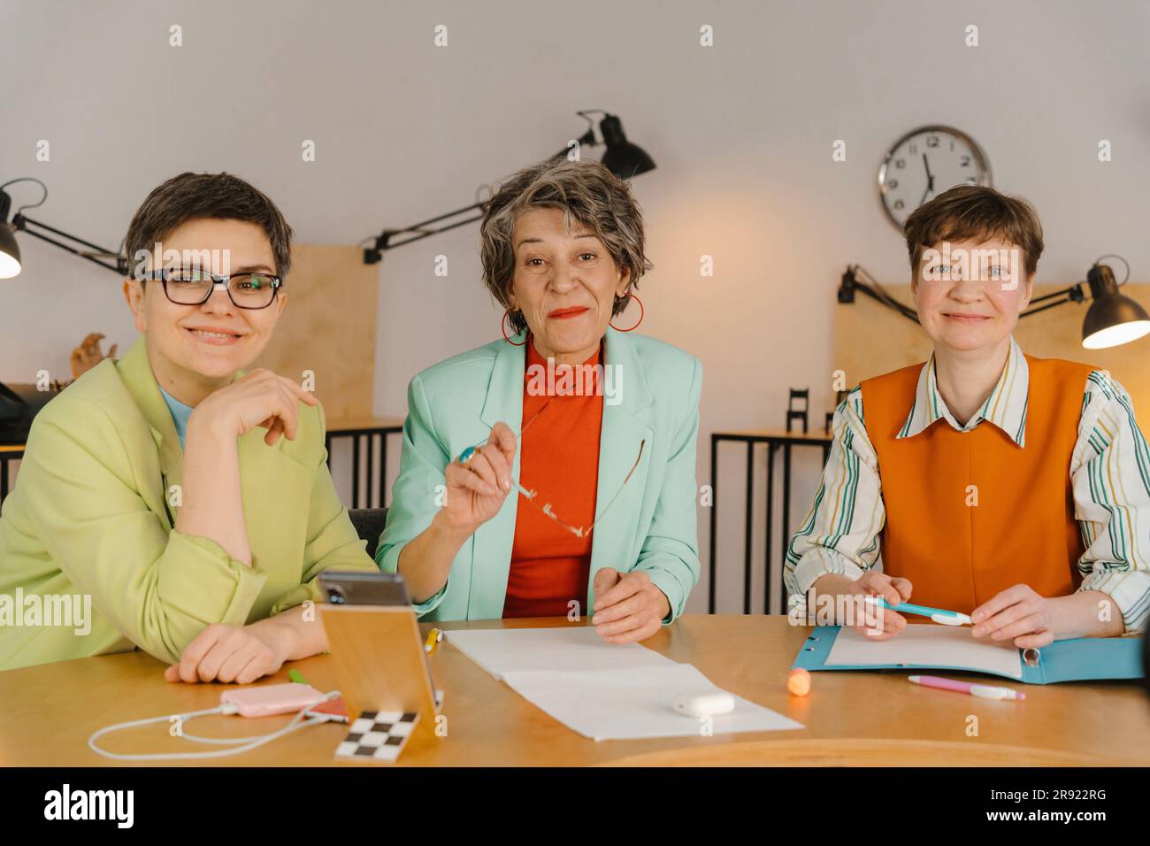 Three business women siting at table looking at camera Stock Photo - Alamy