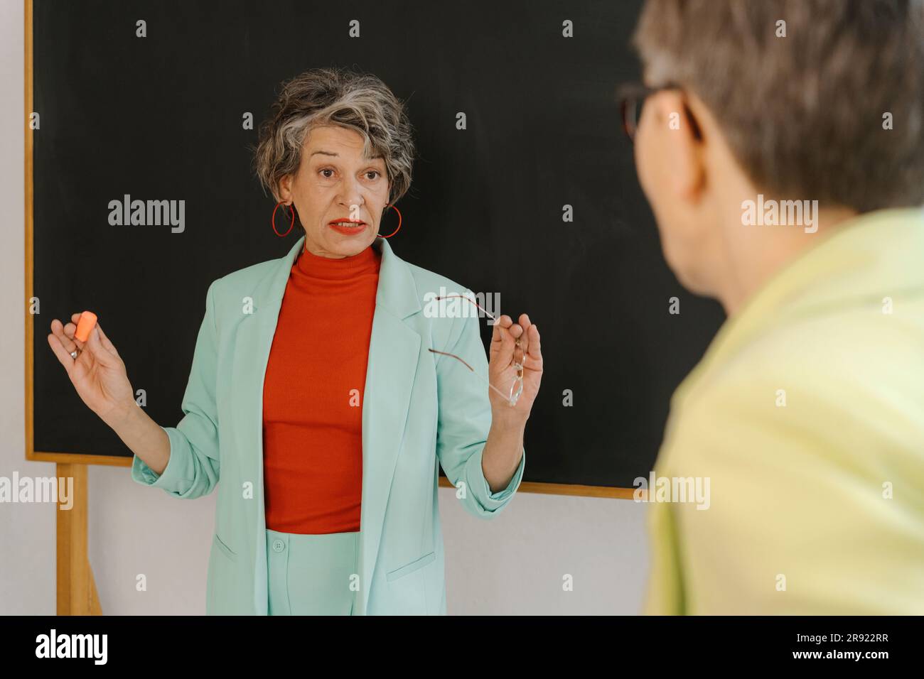 Woman in a bright suit standing in front of blackboard explaining ...