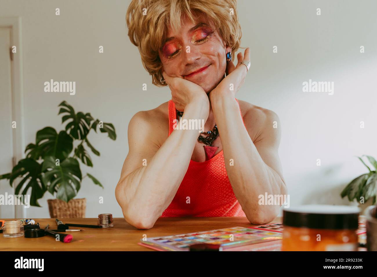 Smiling drag queen leaning on elbows at table in home Stock Photo - Alamy