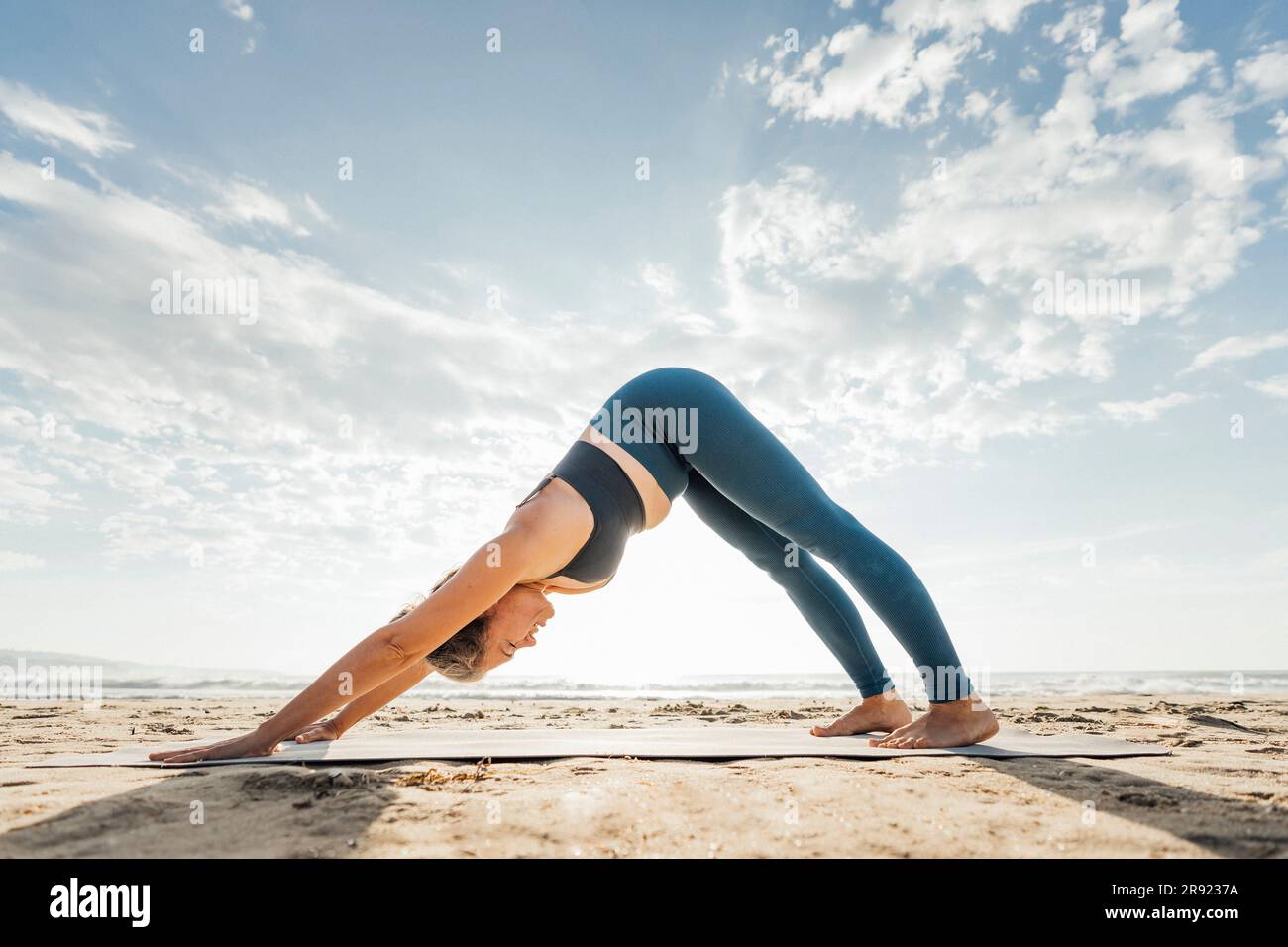 Woman practicing downward facing dog position at beach Stock Photo - Alamy
