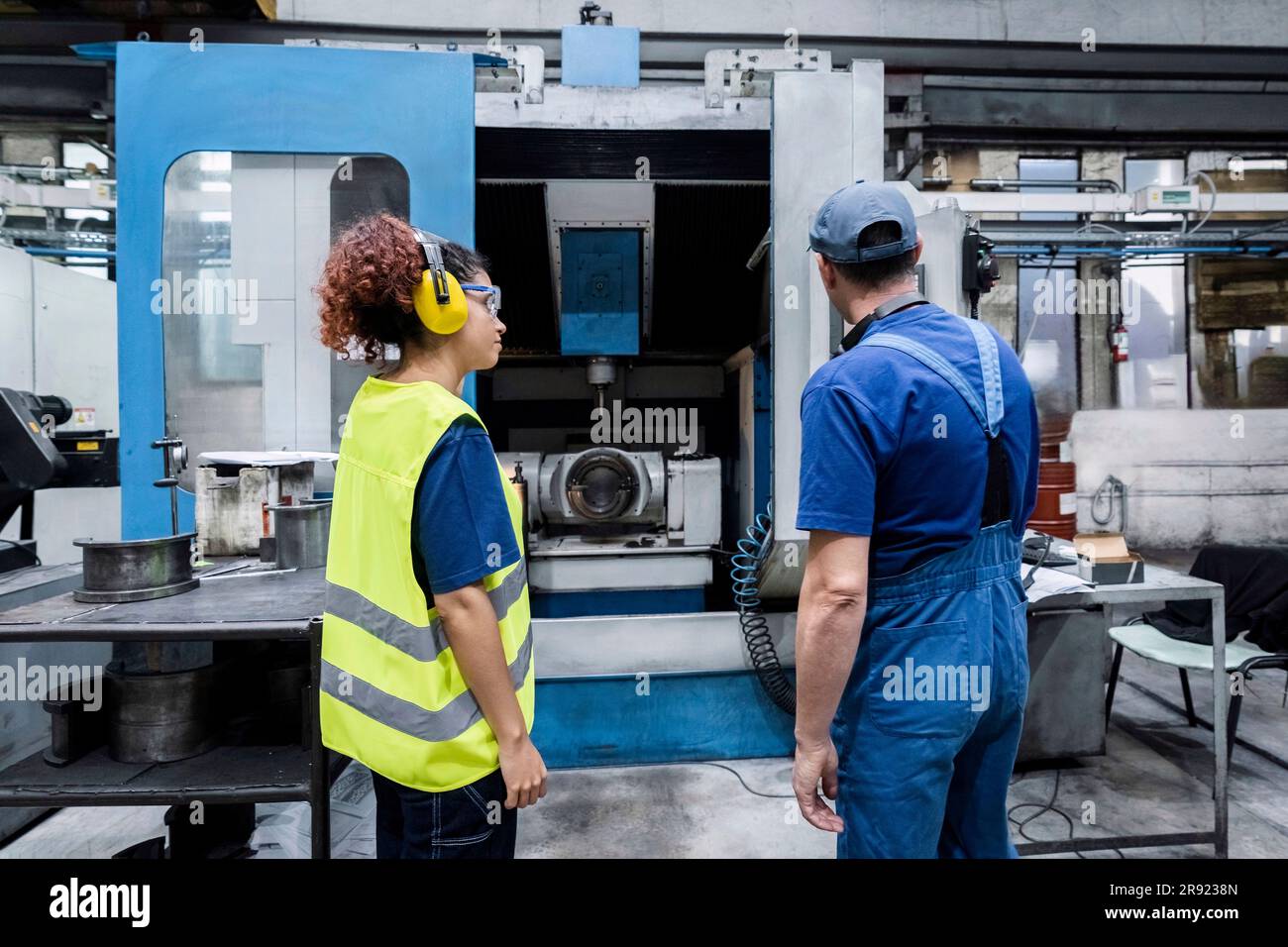 Maintenance engineer examining coworker working on machinery in modern ...