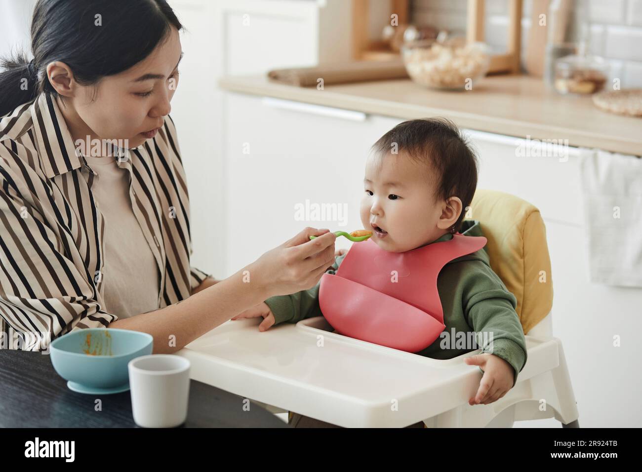 Mother feeding fruit puree to daughter at home Stock Photo - Alamy