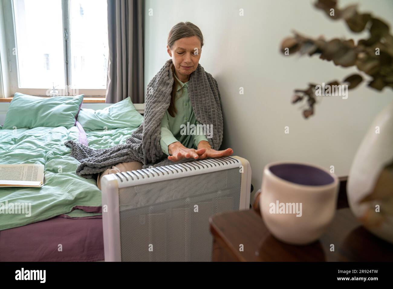 Mature woman warming hands on radiator at home Stock Photo - Alamy