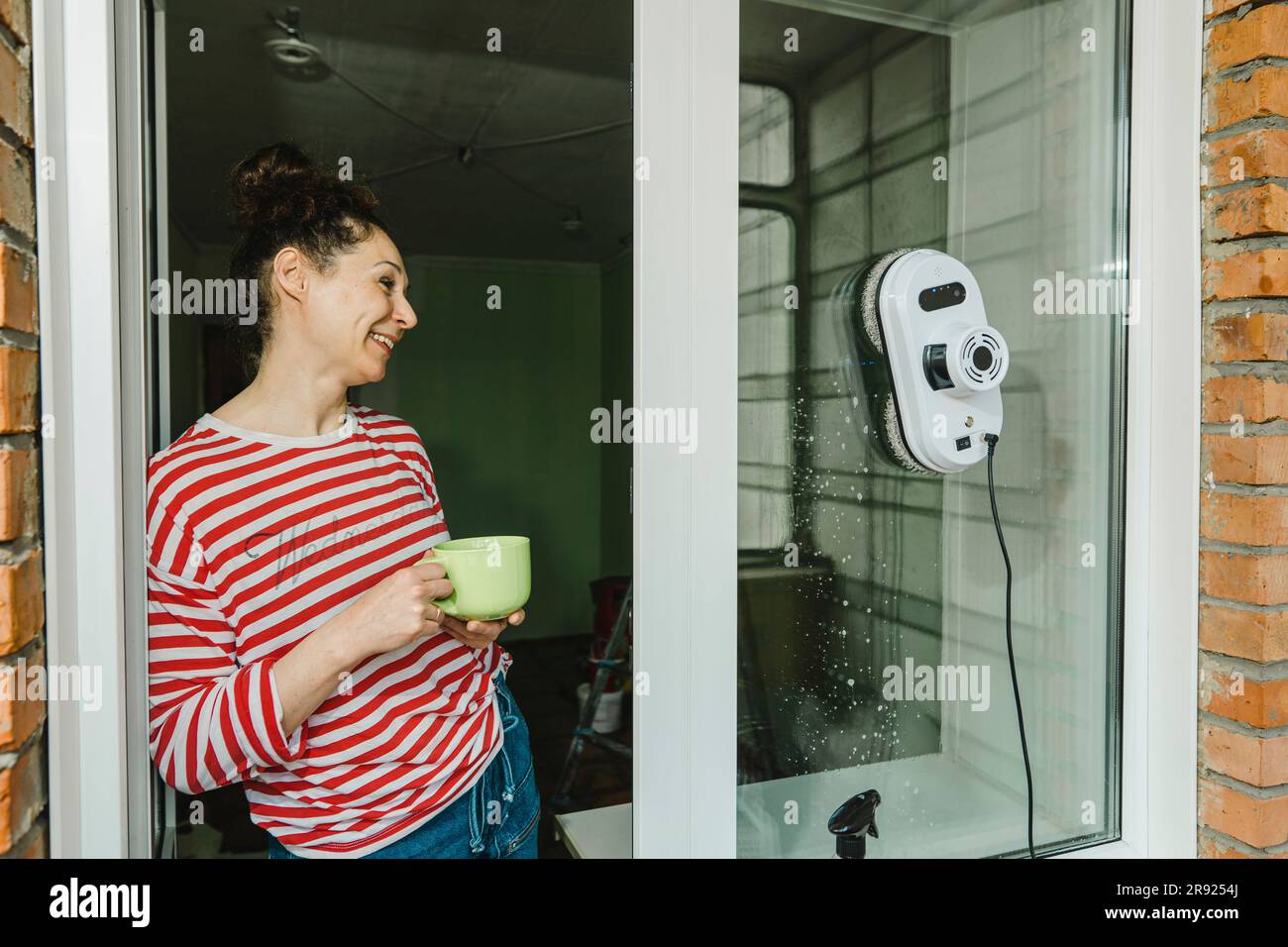 Happy woman with coffee cup cleaning window through robot washer Stock ...