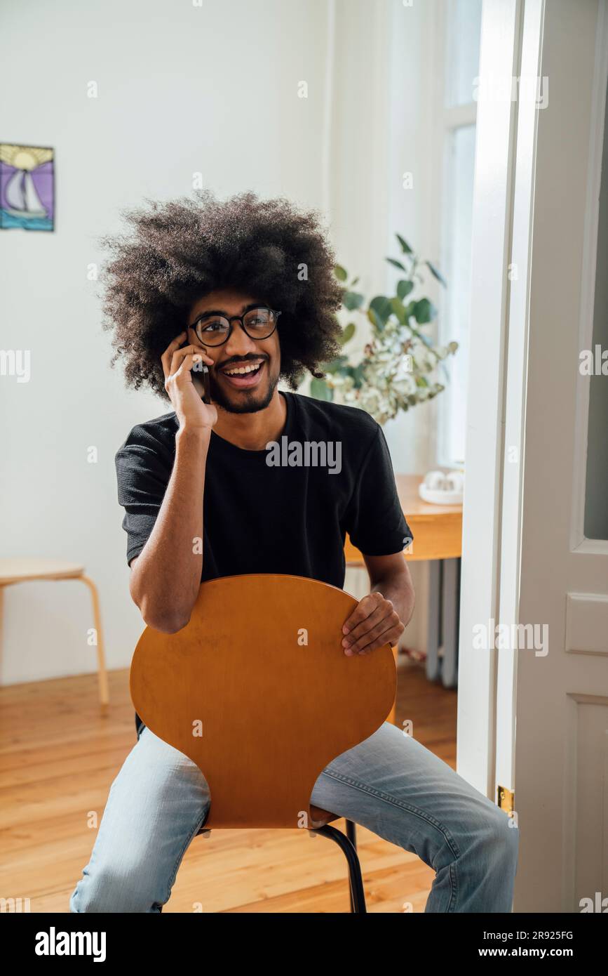 Happy man talking through smart phone sitting on chair at home Stock ...