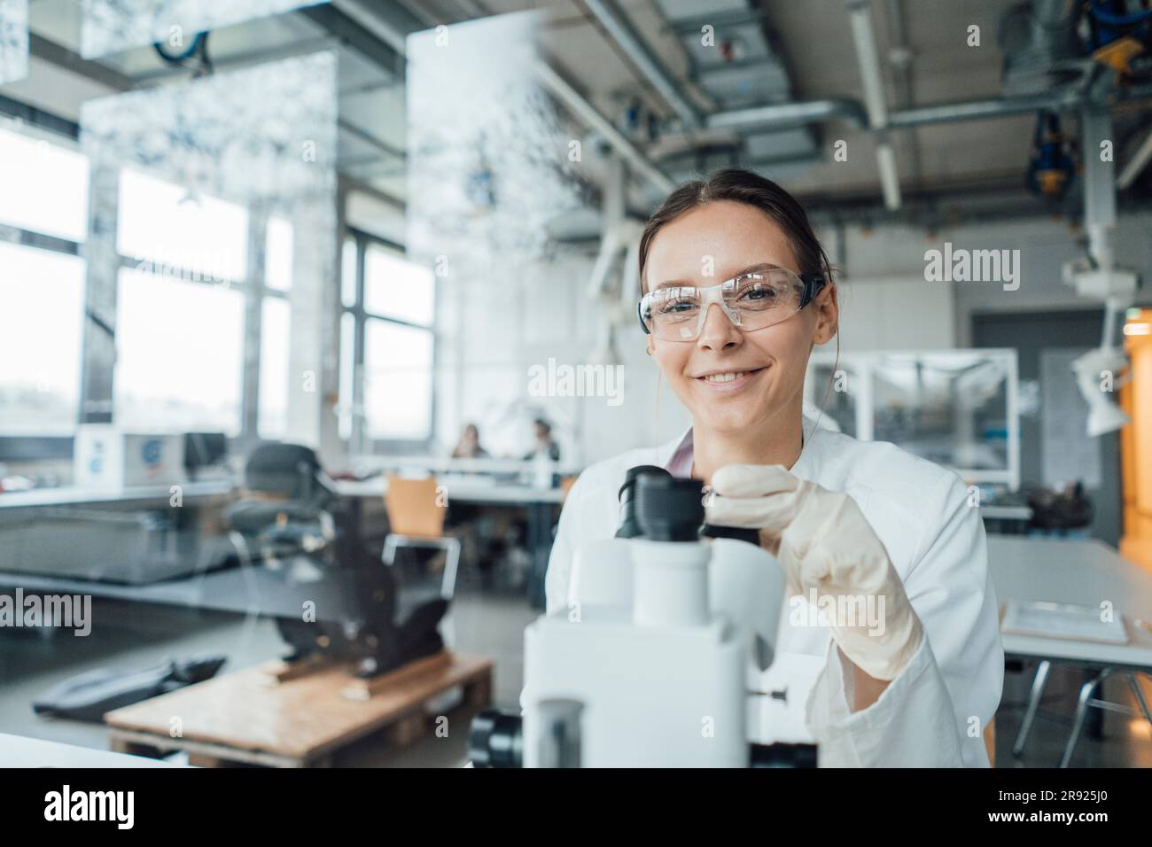 Smiling young scientist with microscope seen through glass Stock Photo ...