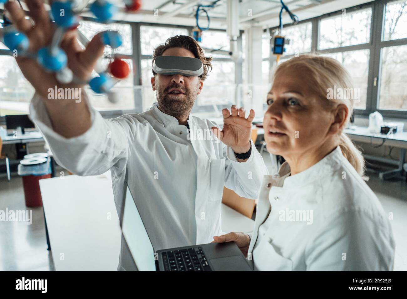 Scientist wearing virtual reality simulator examining molecular structure with colleague Stock ...