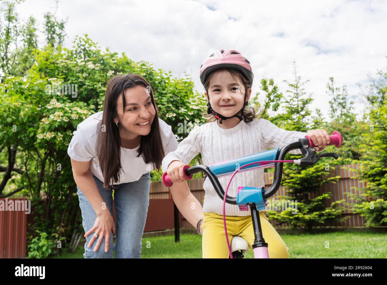 Smiling mother helping daughter riding bicycle in back yard Stock Photo ...