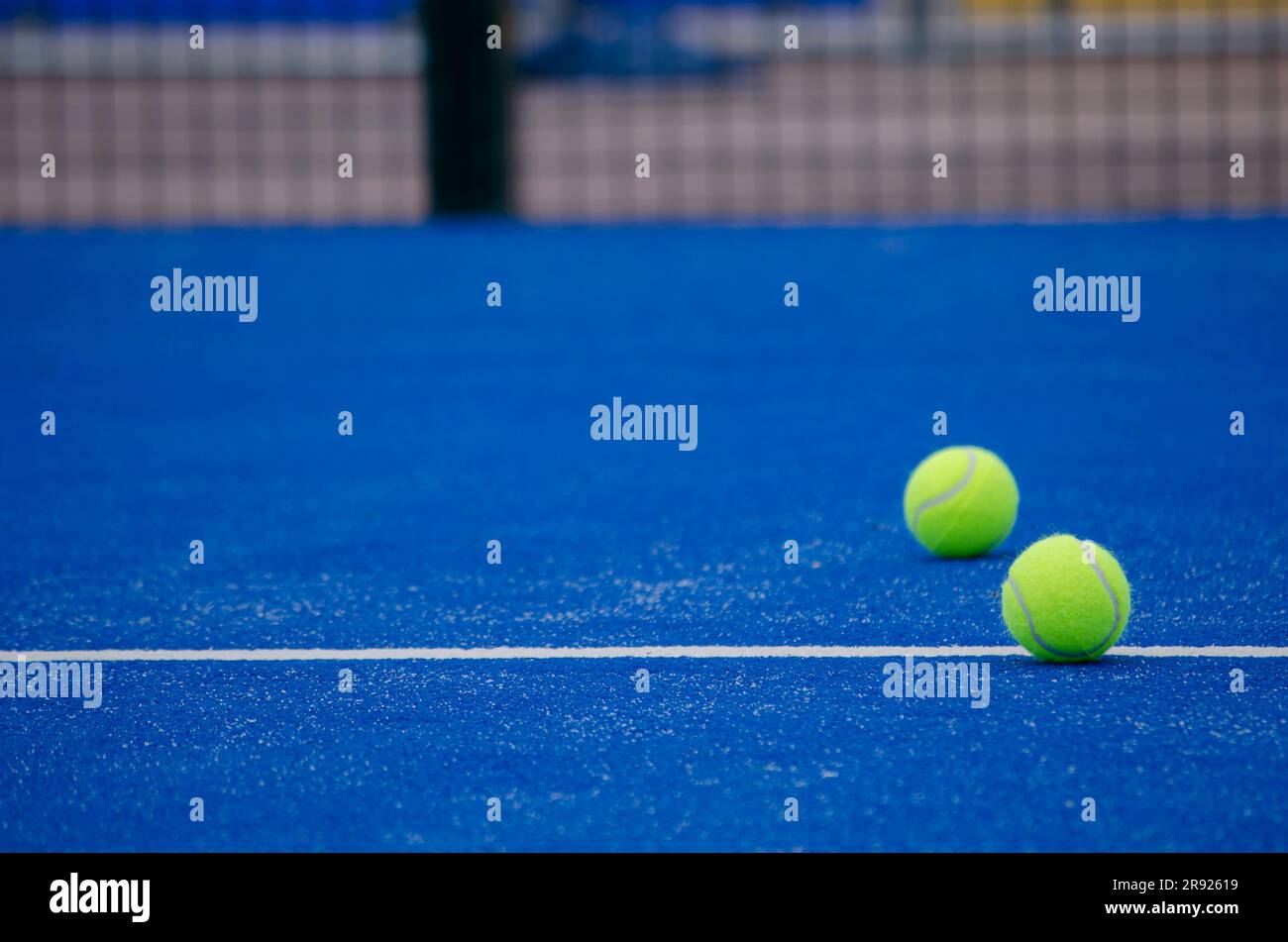 two paddle tennis balls over the line of a blue paddle tennis court ...