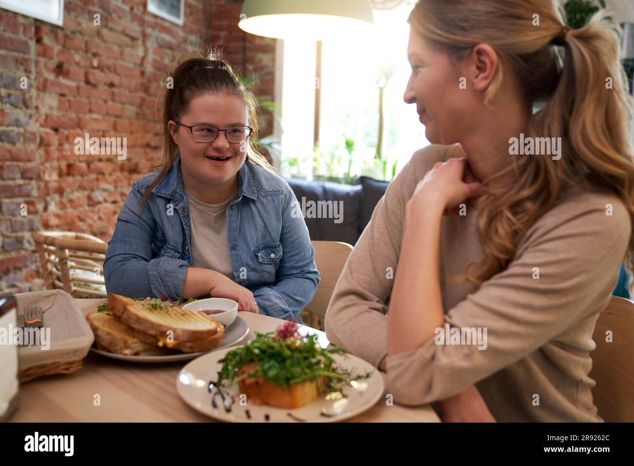 Happy woman with down syndrome having breakfast with friend in cafe ...