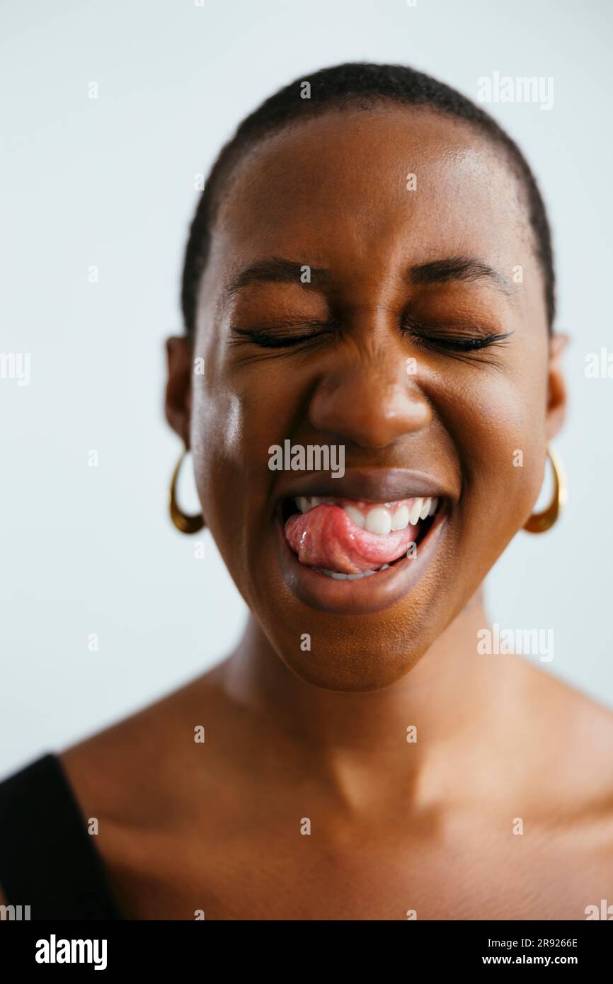 Young woman with short hair sticking out tongue against white ...