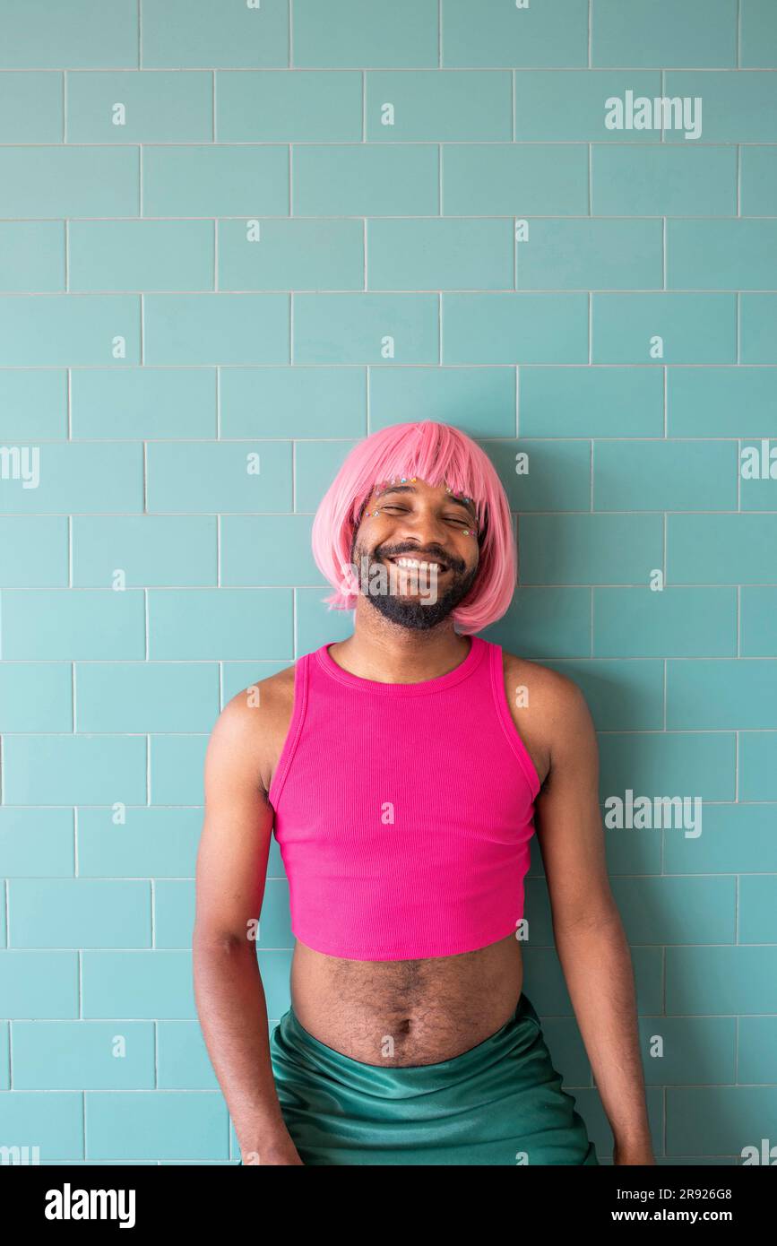 Smiling young queer man standing in front of tiled wall Stock Photo - Alamy