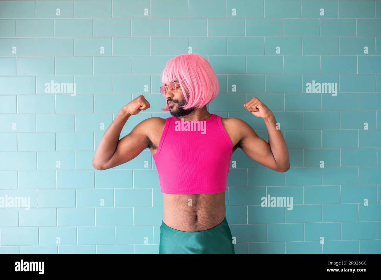 Young queer man flexing muscles in front of tiled wall Stock Photo - Alamy