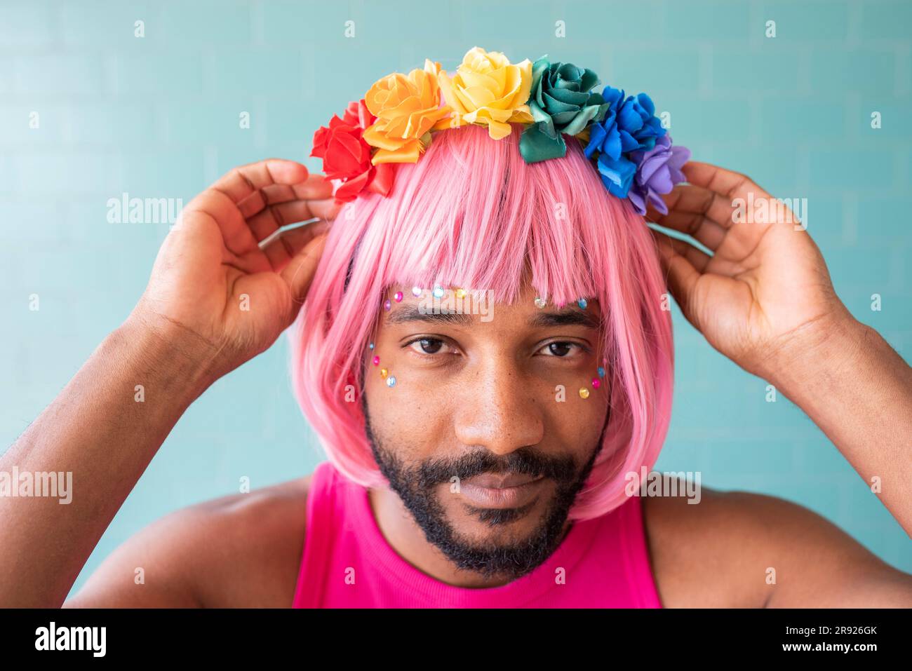 Young queer man adjusting flower tiara in front of wall Stock Photo - Alamy