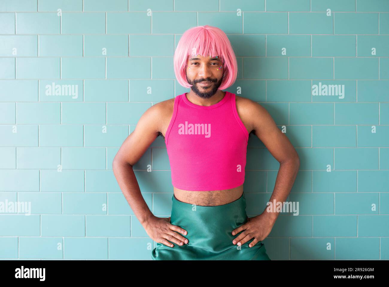 Young queer man standing with arms akimbo in front of tiled wall Stock ...
