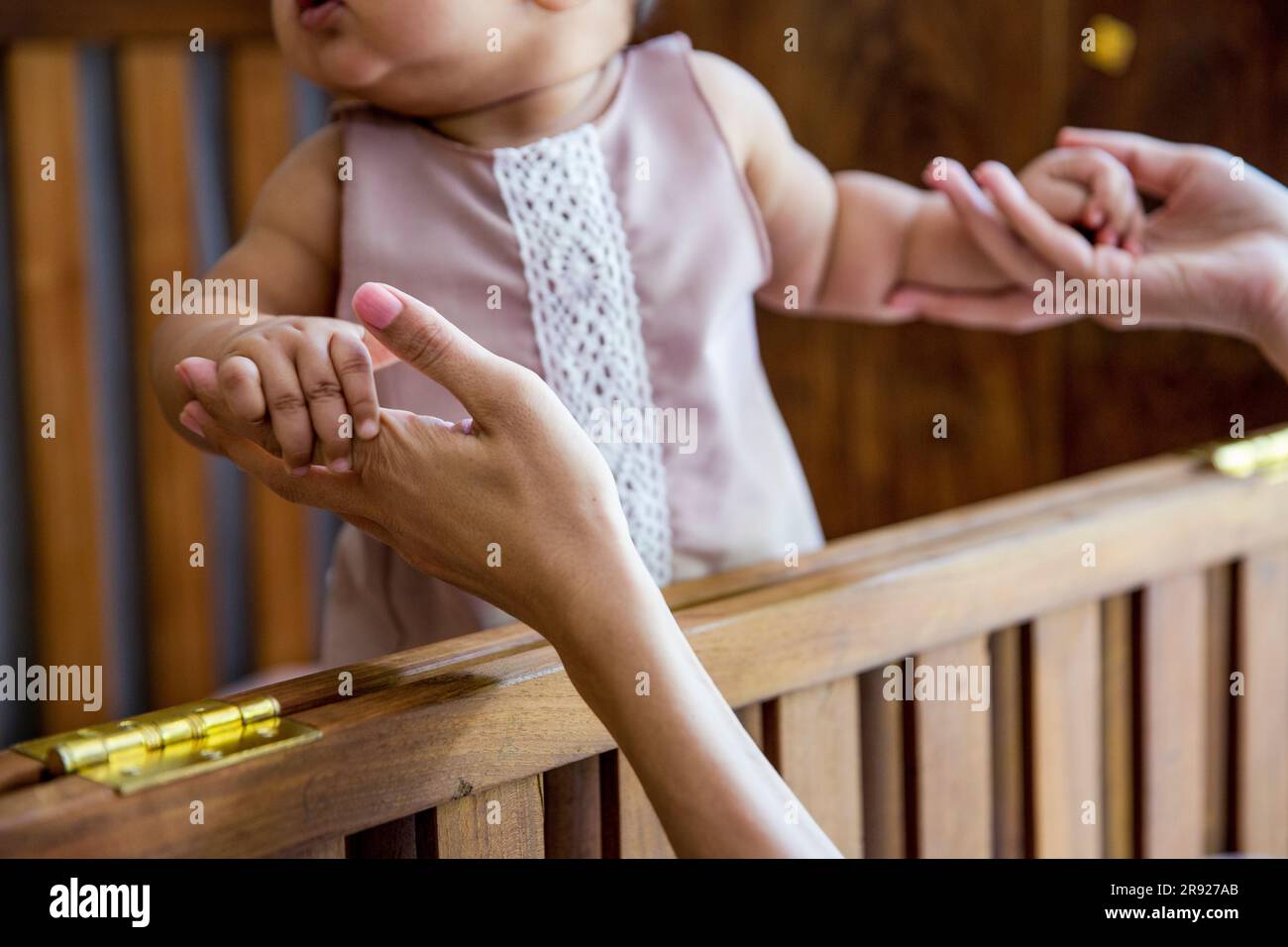 Mother holding hands of baby daughter standing in crib Stock Photo - Alamy