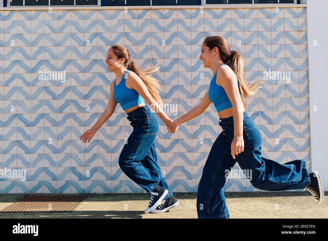 Sisters holding hands and running in front of wall Stock Photo - Alamy