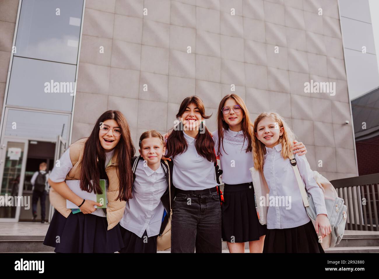 Happy friends with arm around each other standing in front of school ...