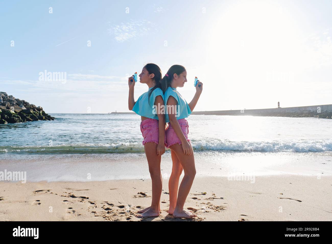 Twin Sisters In Matching Outfits Standing Back To Back With Squirt Guns